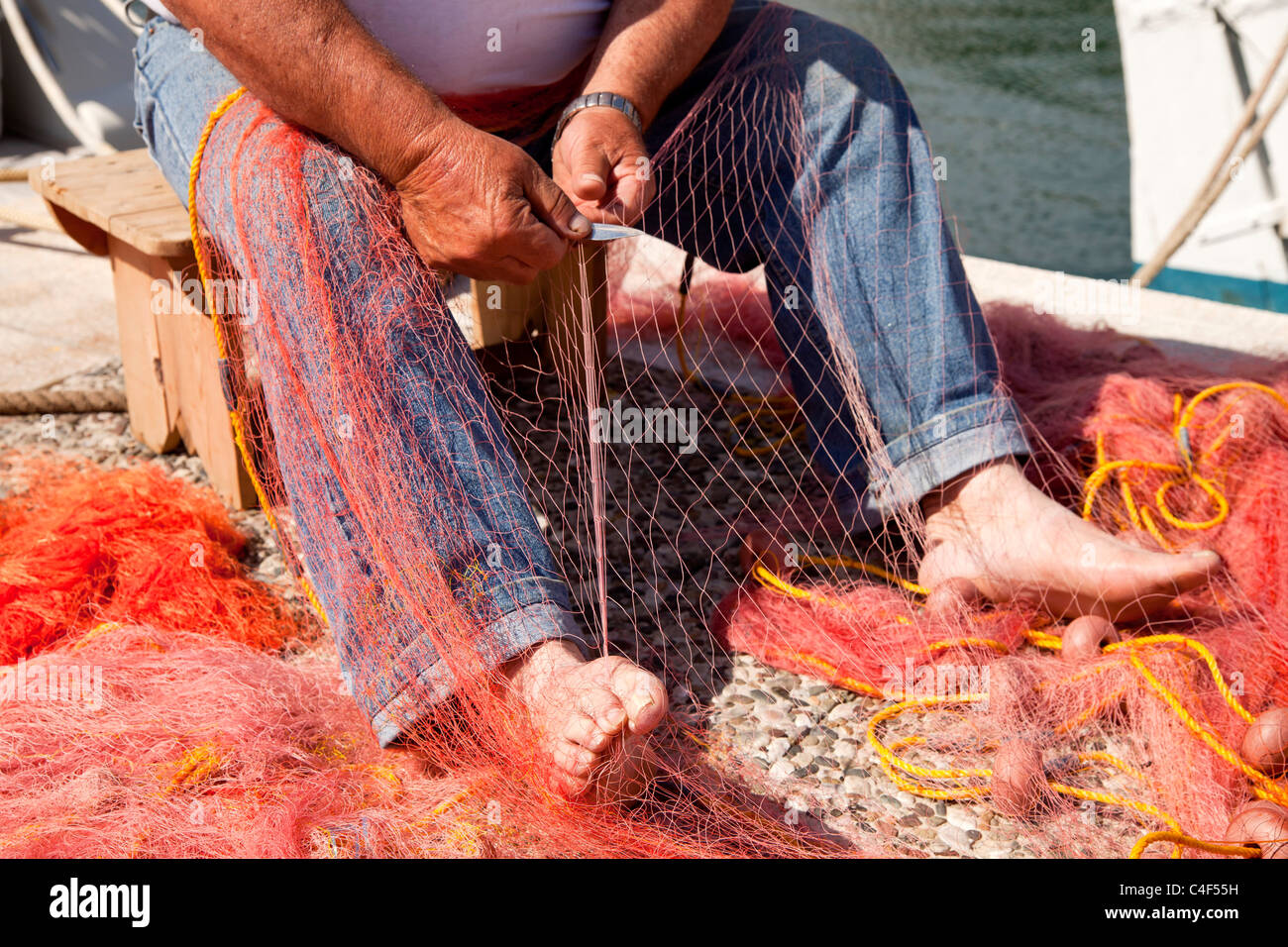 elderly fisherman repairing his net at the old harbour of Skiathos Town ...