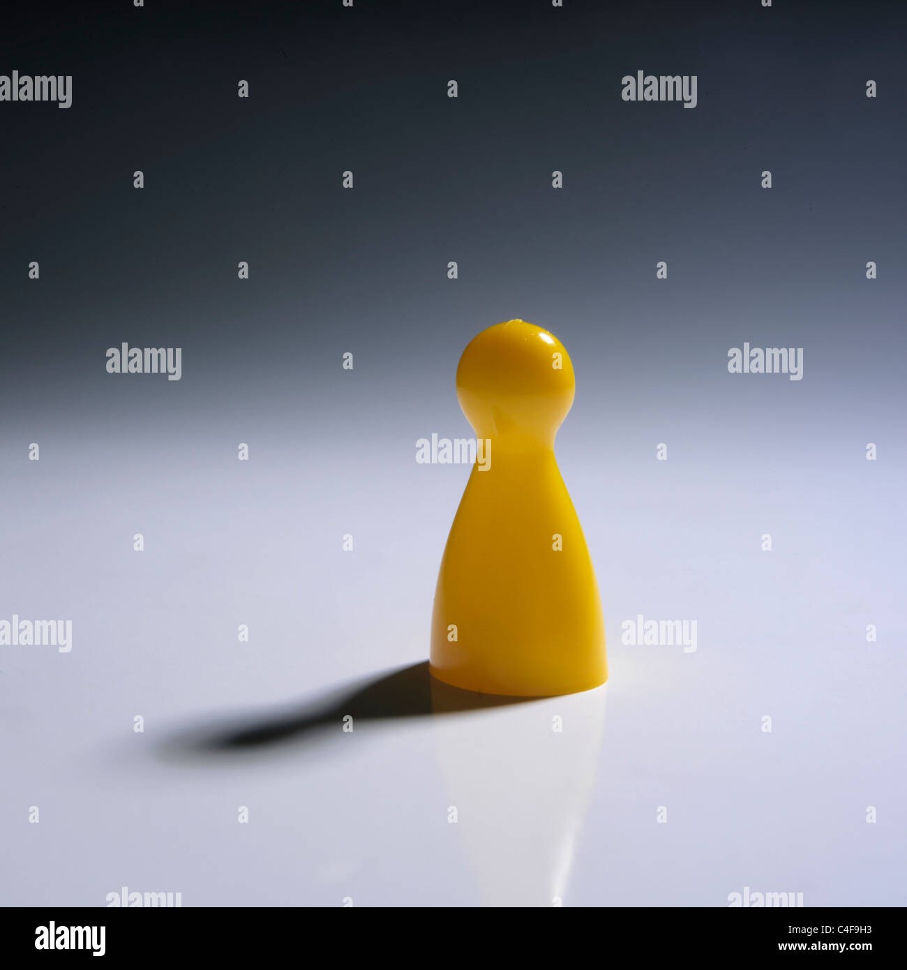 Yellow game piece stands alone on a reflective surface in a minimalist ...