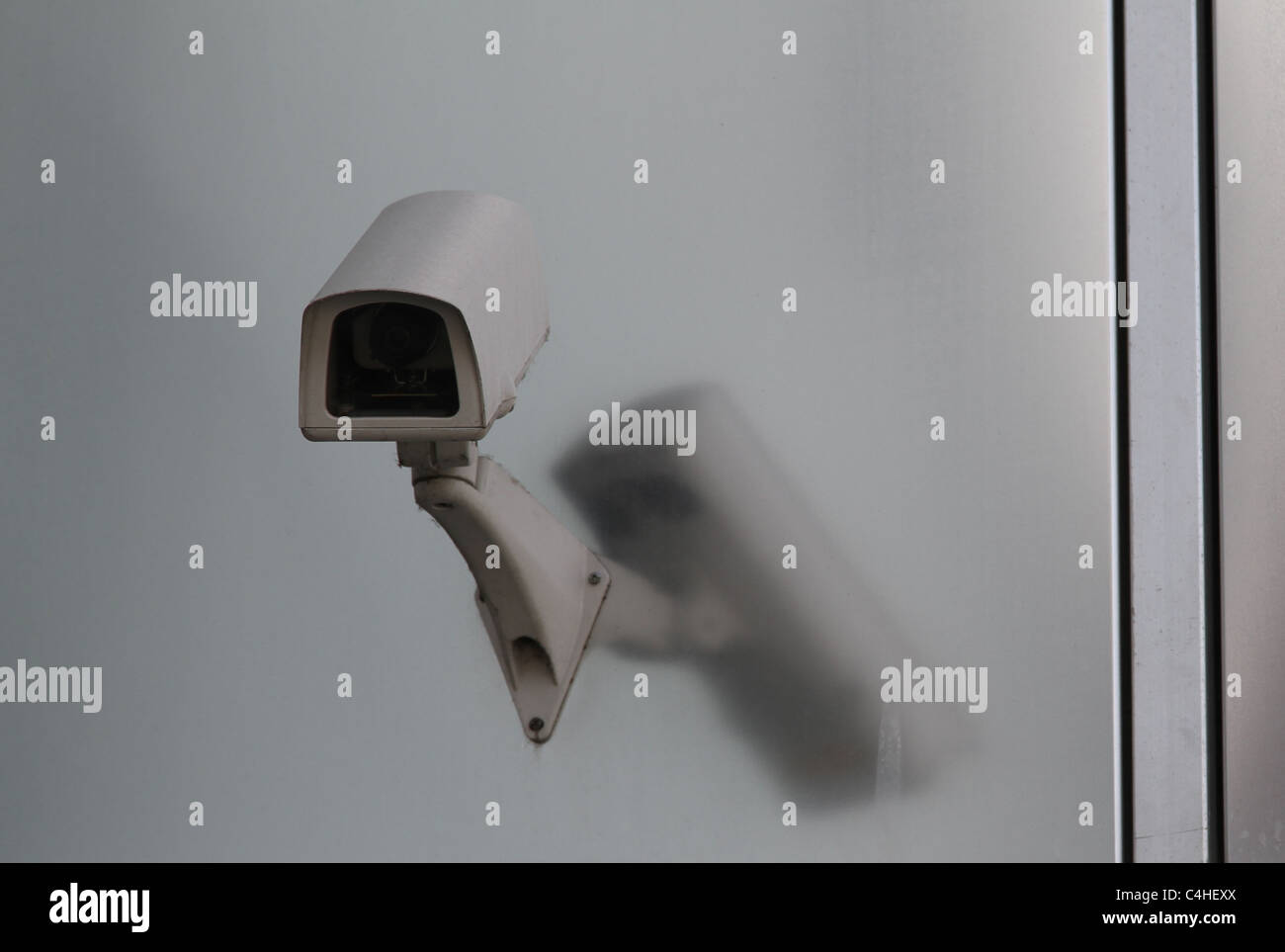 white cctv camera mounted on and reflected in a stainless steel facade ...