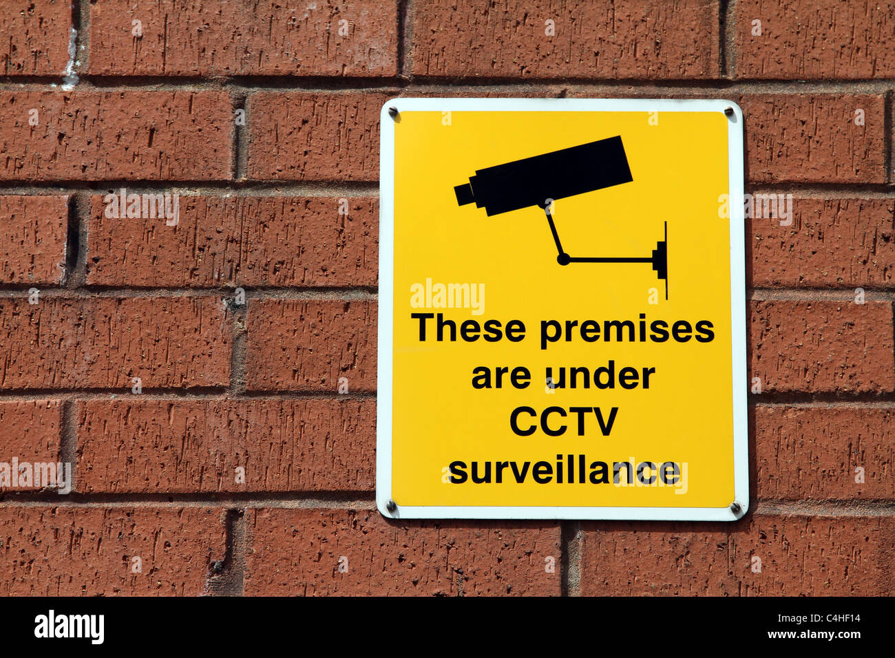 yellow premises under CCTV surveillance sign on a red brick wall Stock ...