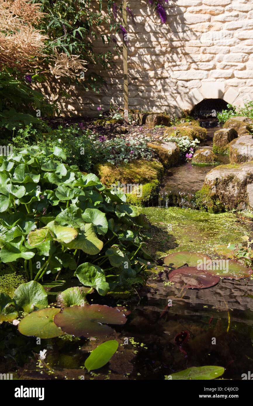 UK gardens. Garden pond water feature with a small stream flowing under ...