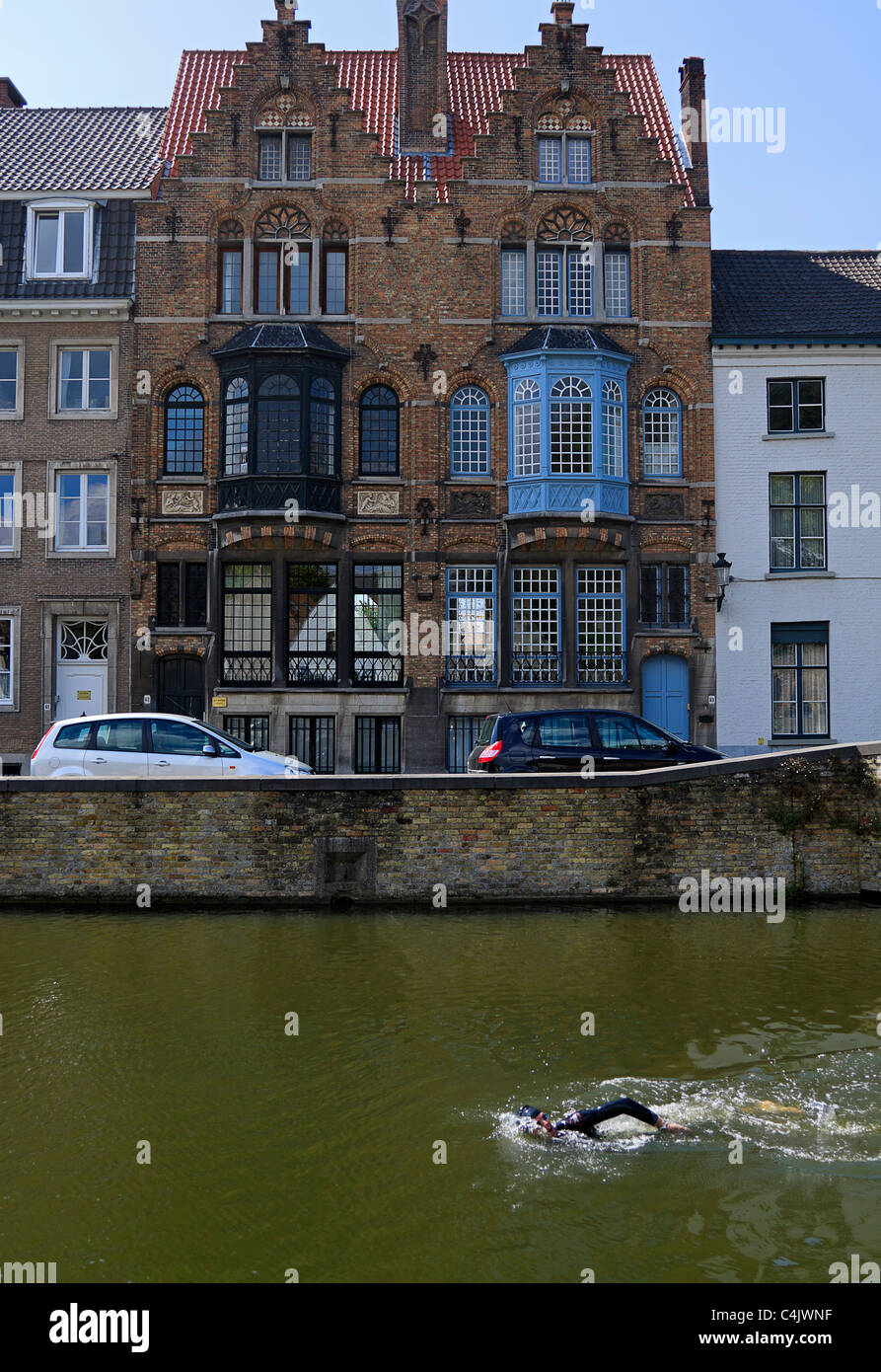 Canalside houses on Langerei, Bruges, Belgium. A swimmer is practising ...