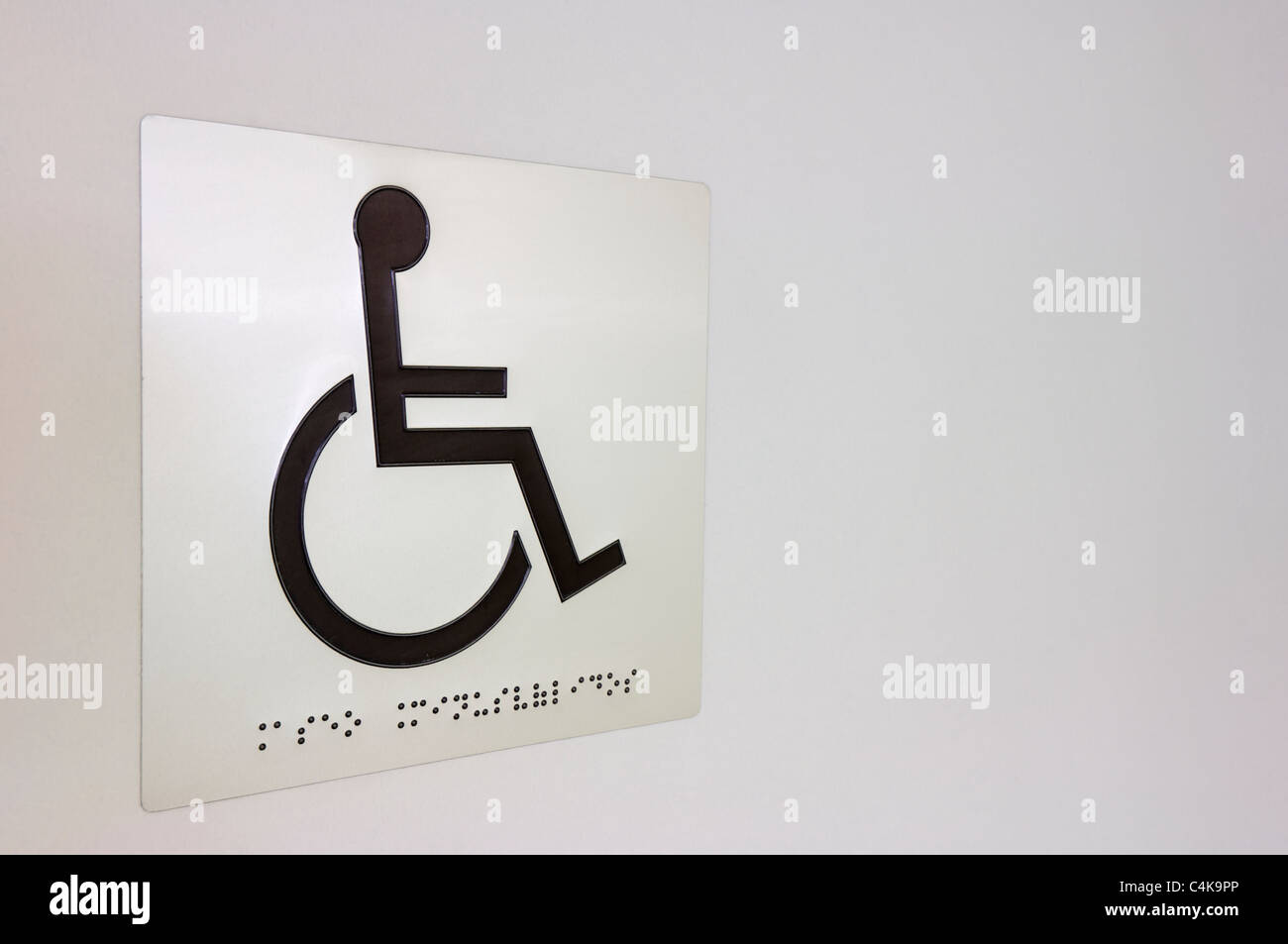 Sign indicating handicapped zone on a white wall and writing Braille ...