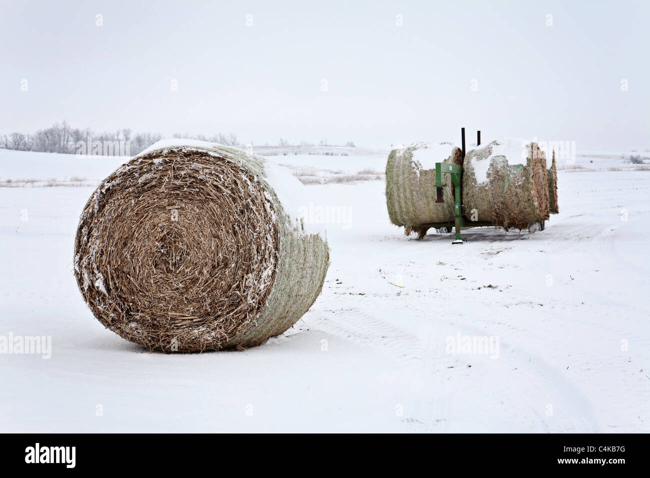 One large round bale sitting on ground in snow in front of a loaded ...