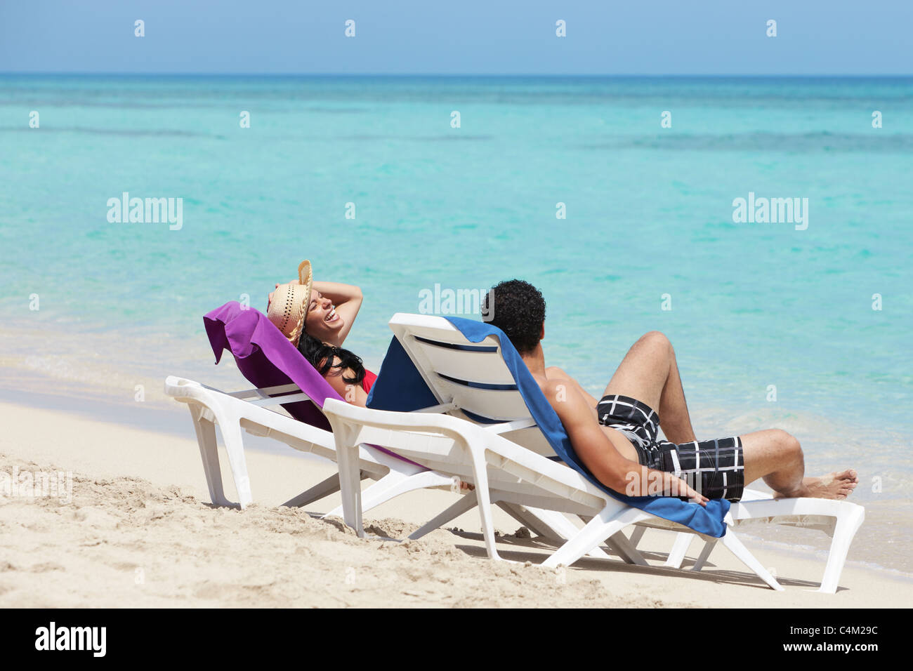 husband and wife relaxing on sunbeds on the beach and smiling ...