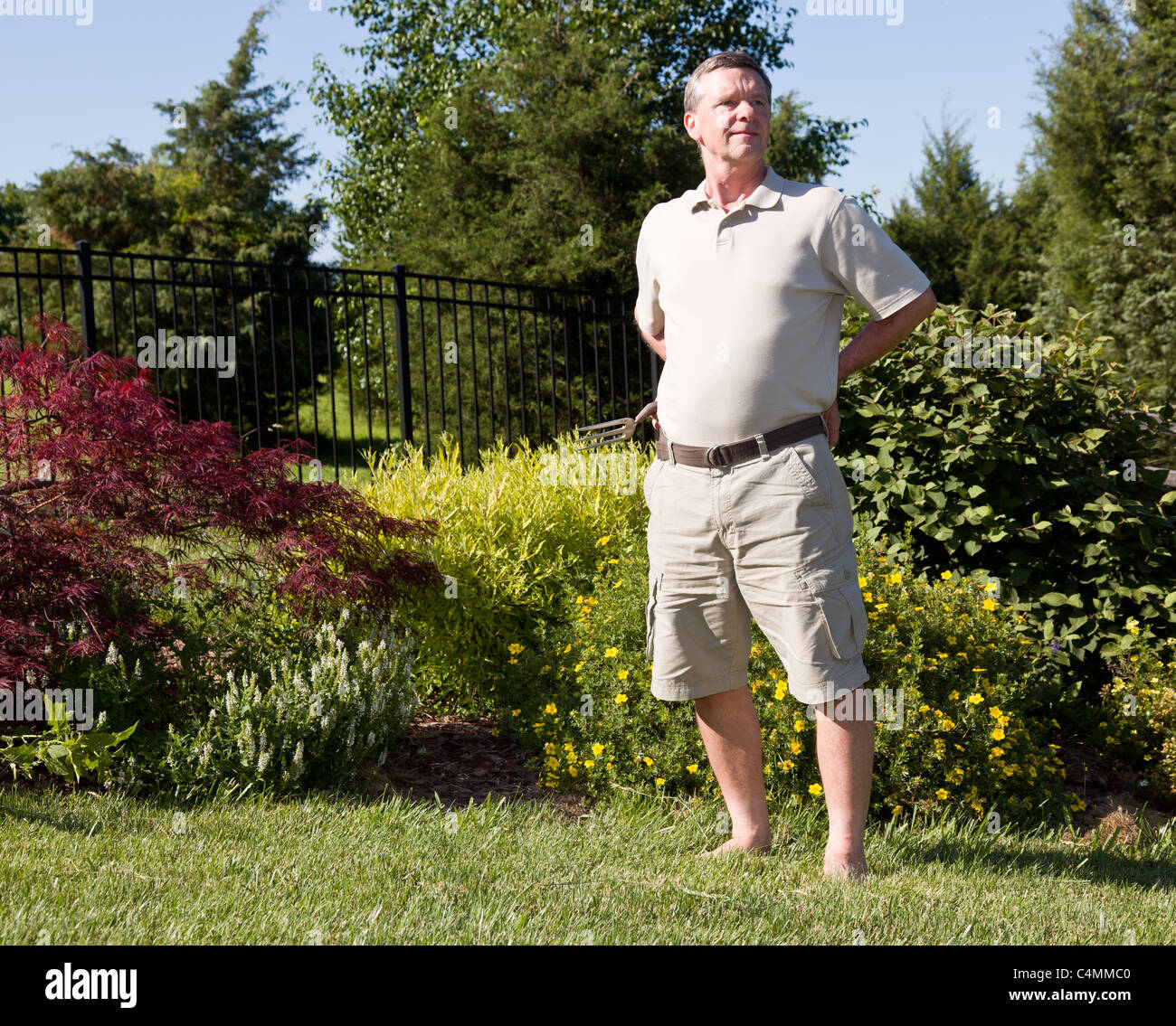 Baby boomer sitting on the grass lawn and digging for weeds in a ...