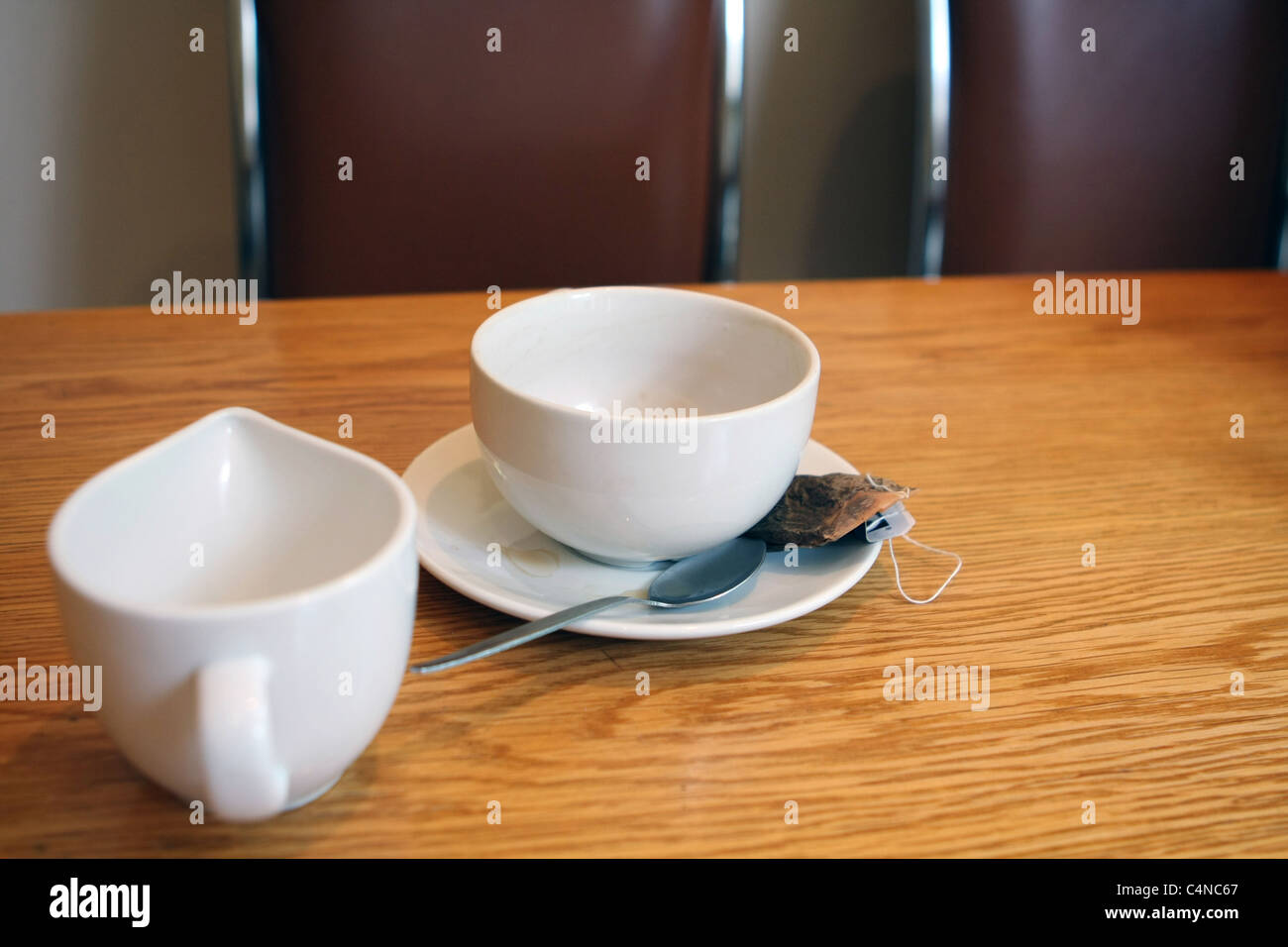 A cup, spoon and used tea bag on a saucer next to a milk jug Stock ...