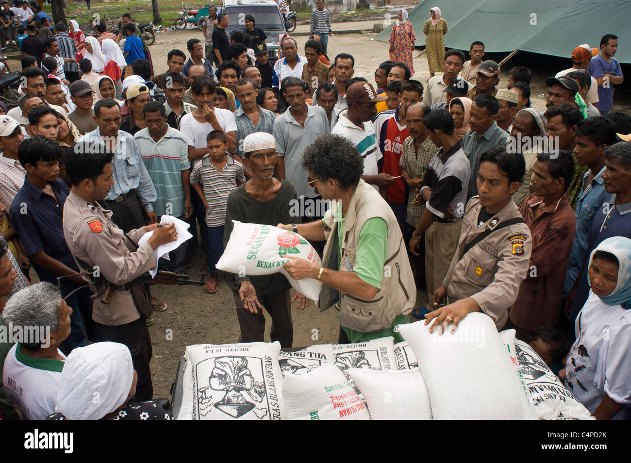 An NGO worker hands out sacks of rice to people displaced from their ...