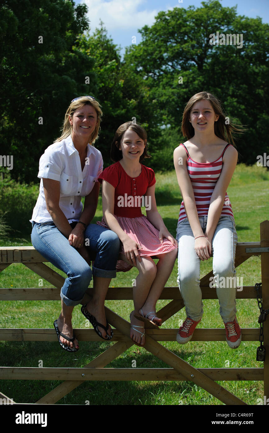 Portrait of a woman and two girls sitting on a wooden gate Stock Photo ...