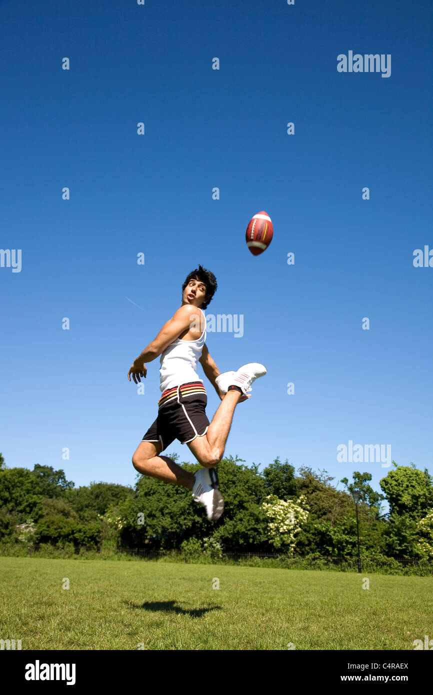 Man jumping playing with oval ball in park Stock Photo - Alamy