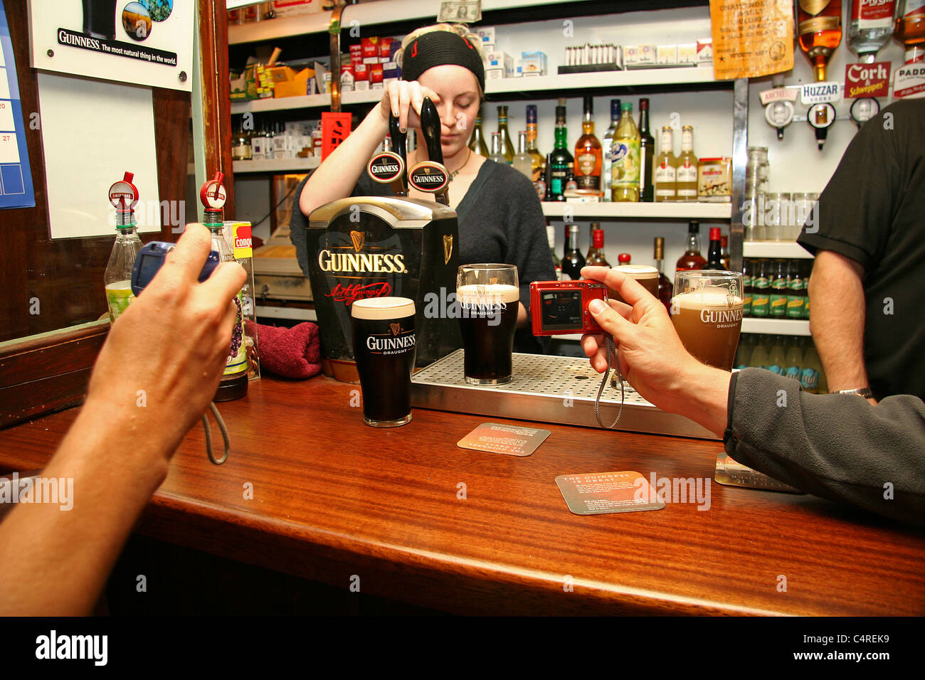 Tourists photographing woman pouring a pint of Guinness at a local pub ...