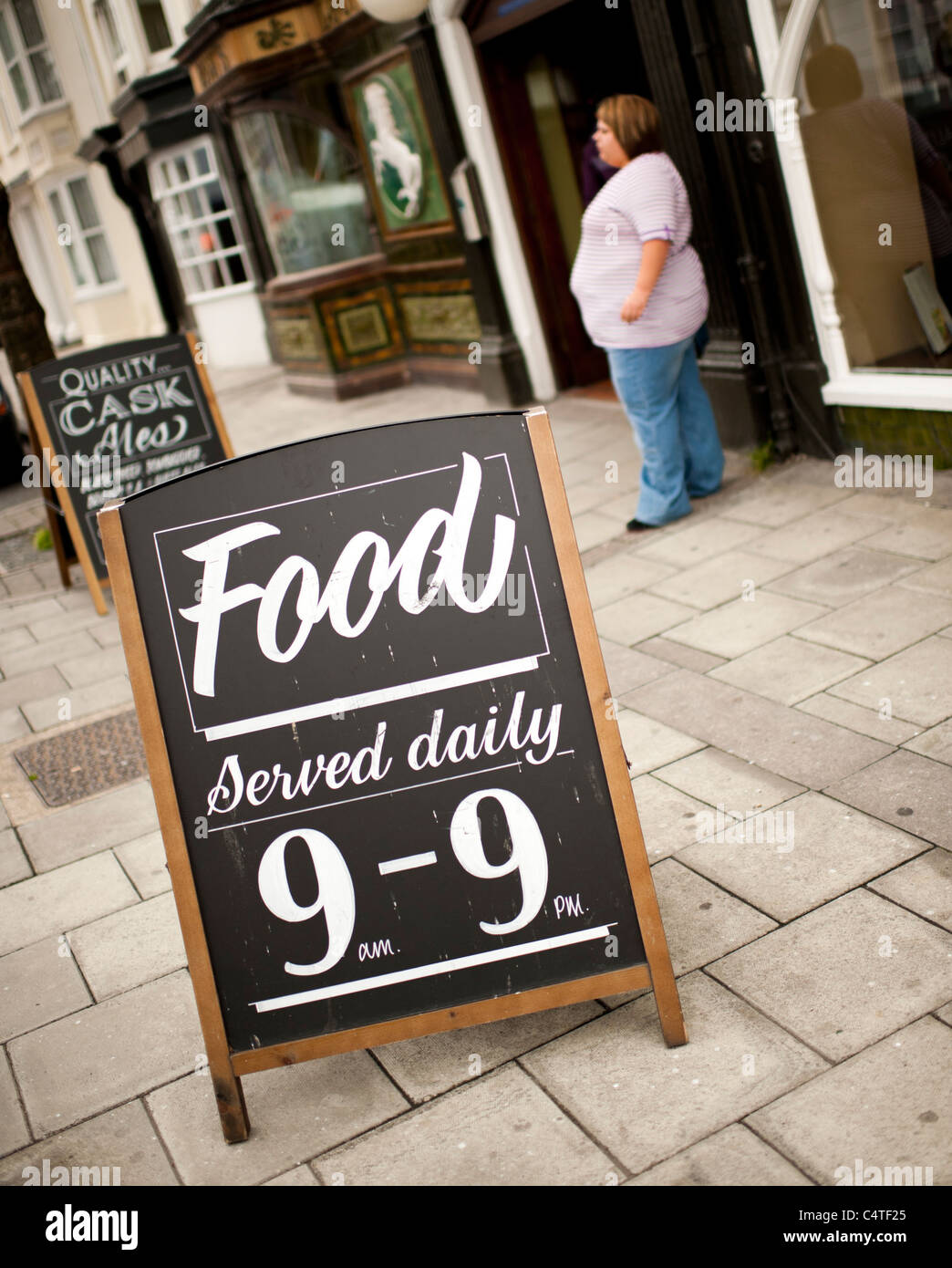 "Food served daily sign" outside pub, large woman out of focus in ...
