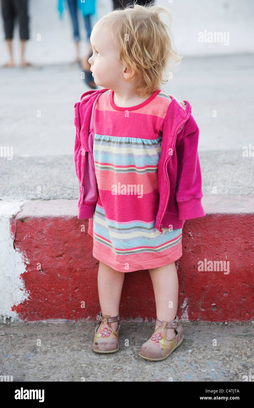 Toddler girl standing on sidewalk, looking over her shoulder Stock ...
