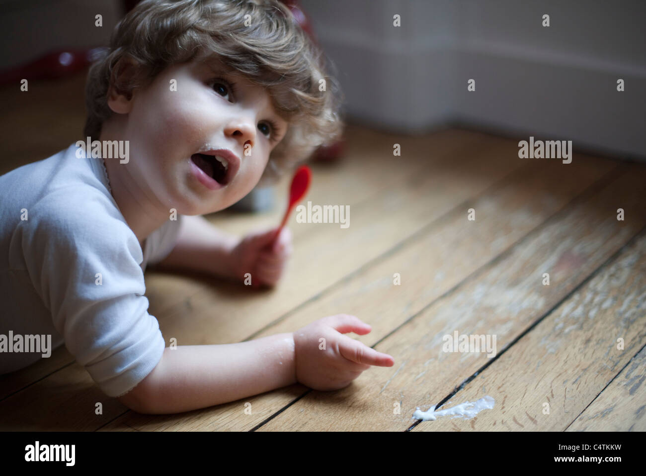 Toddler lying on floor with spoon in hand, pointing to spilled food ...