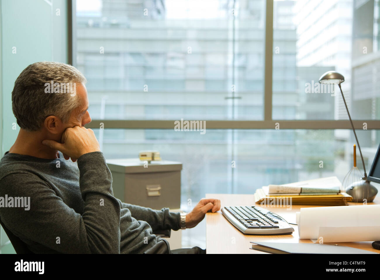 Man sitting at desk in office, looking away in thought Stock Photo - Alamy