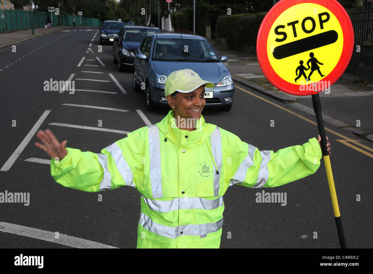 A lollipop lady stops traffic to help school children across the road ...