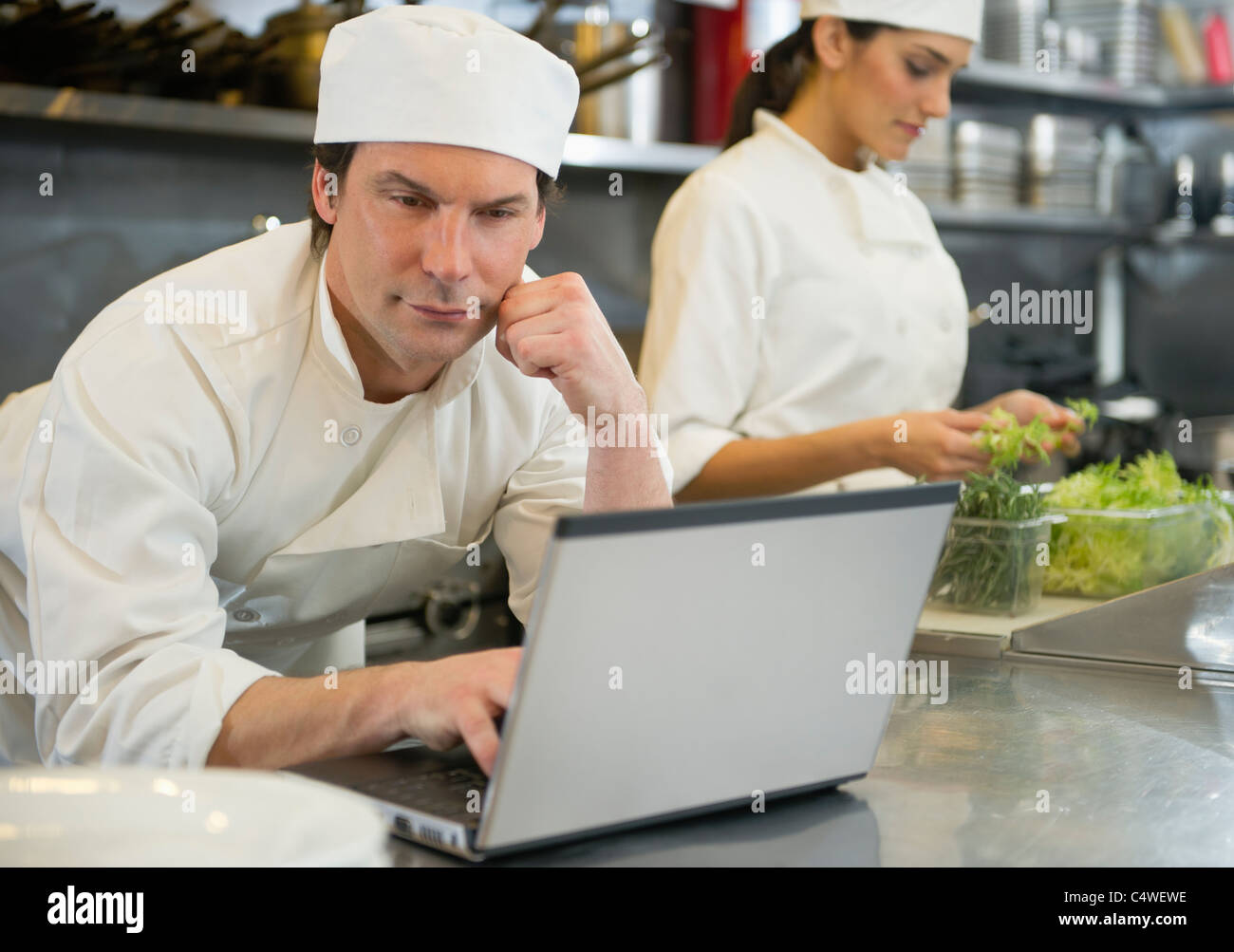 USA, New York, New York City, Chef using laptop and cook preparing food ...