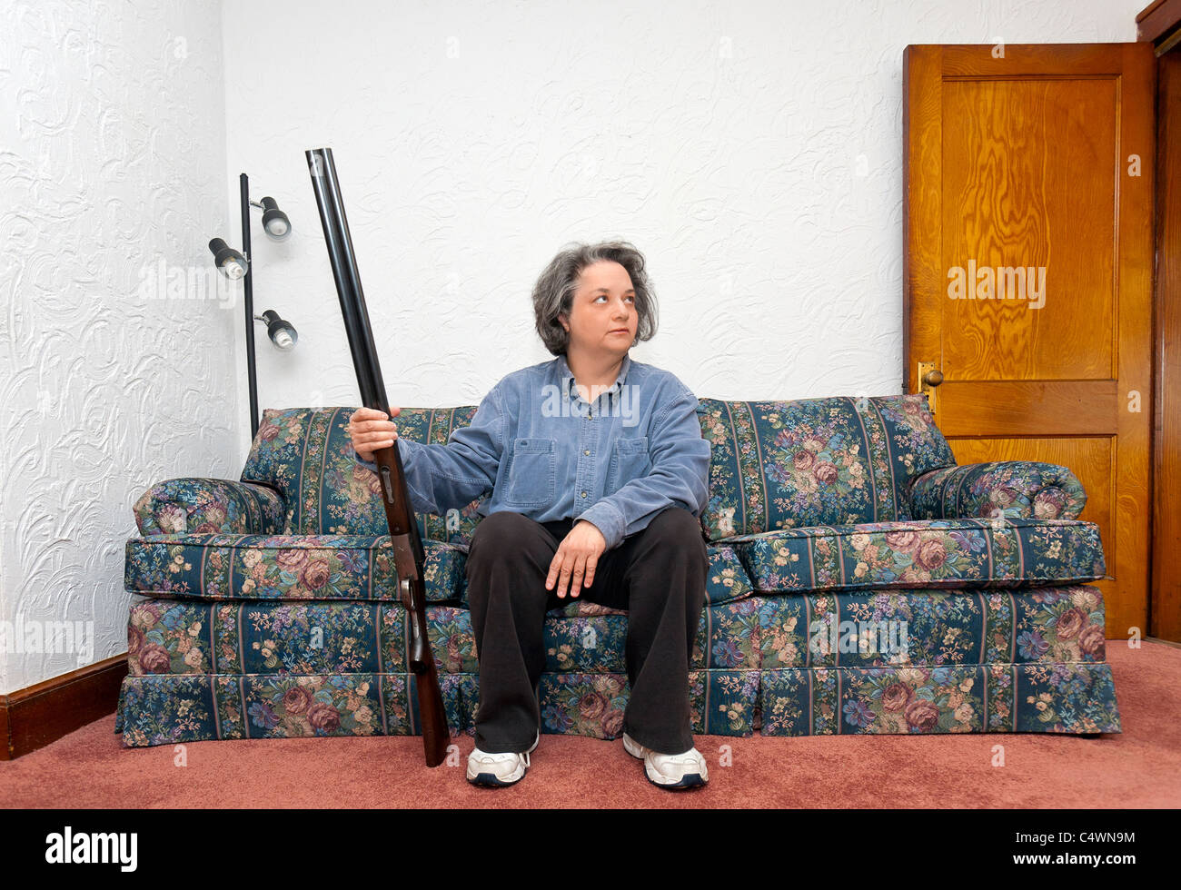 Middle aged Woman sitting on sofa holding a shotgun Stock Photo - Alamy