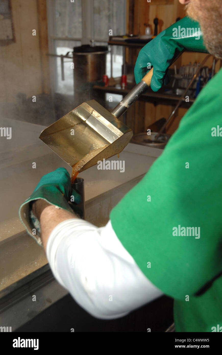 Maple syrup drips from a ladle in the process of boiling maple sap into ...