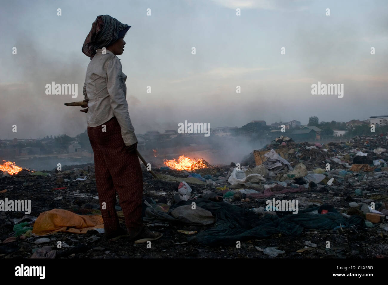 A woman worker is watching piles of burning trash at a toxic and ...