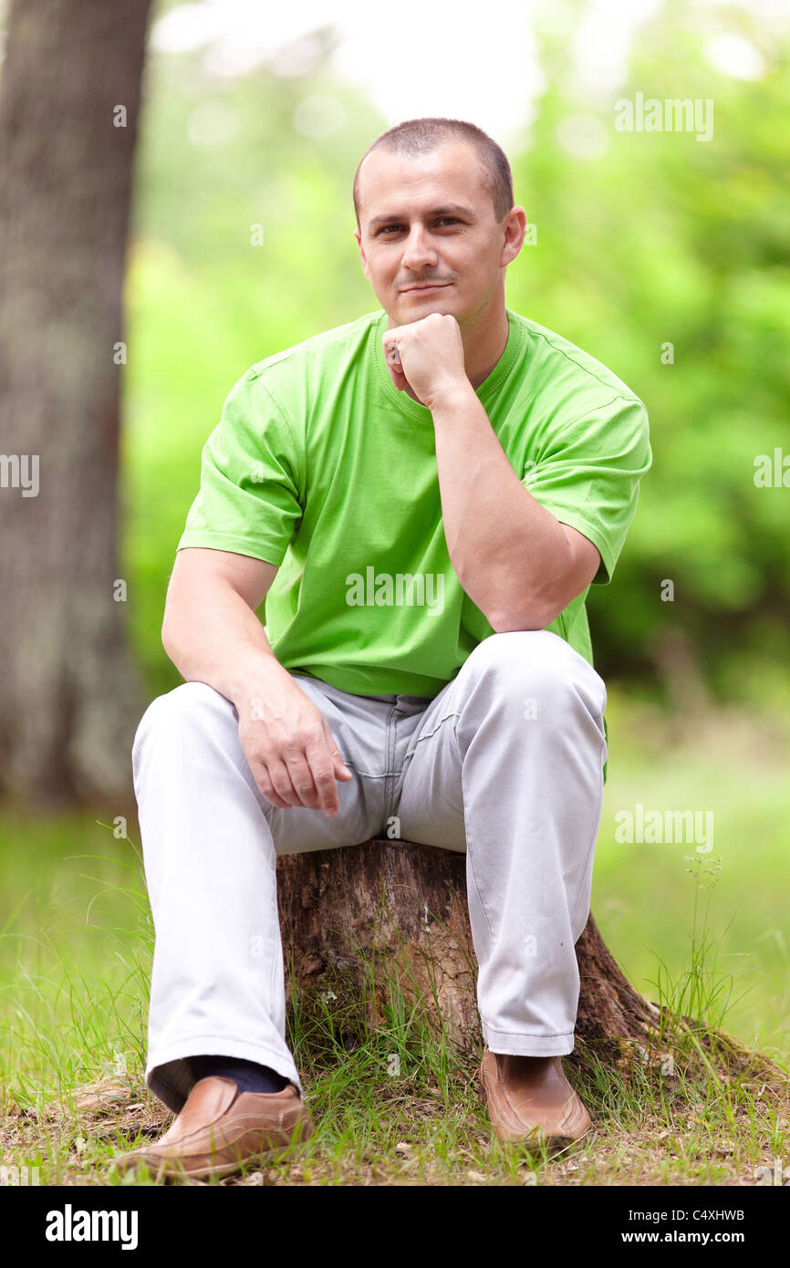 Portrait of a young man sitting on a tree stump in the forest Stock ...