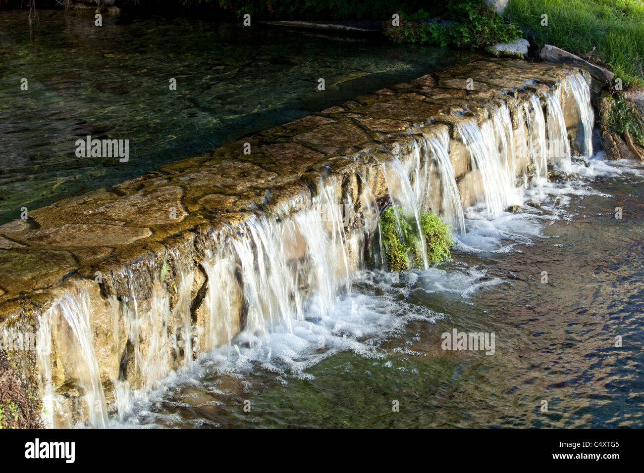 Clear spring water flows over low waterfall into small spring-fed lake ...