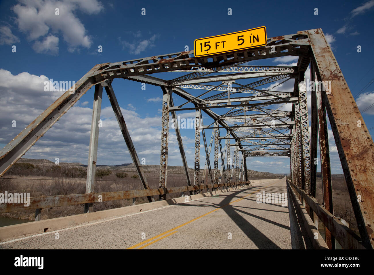 A small steel through-truss bridge spans the Pecos River on a two-lane ...