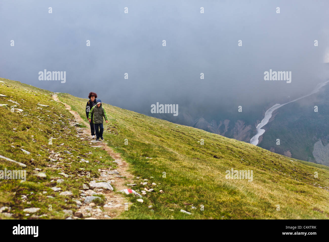 Mother and son hiking into the mountains, on a steep trail with heavy ...