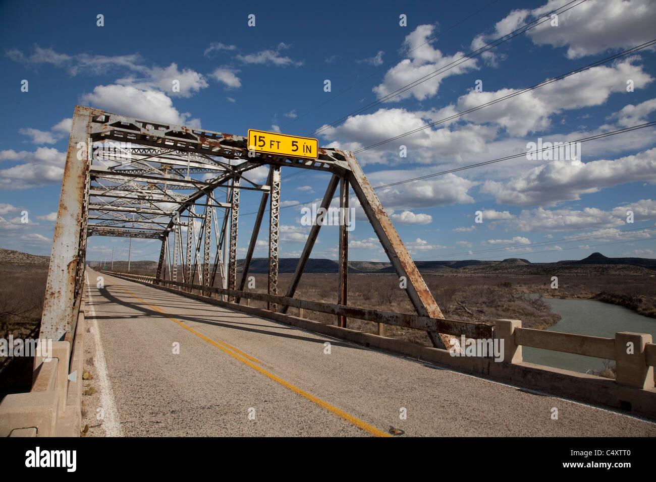 A small steel through-truss bridge spans the Pecos River on a two-lane ...