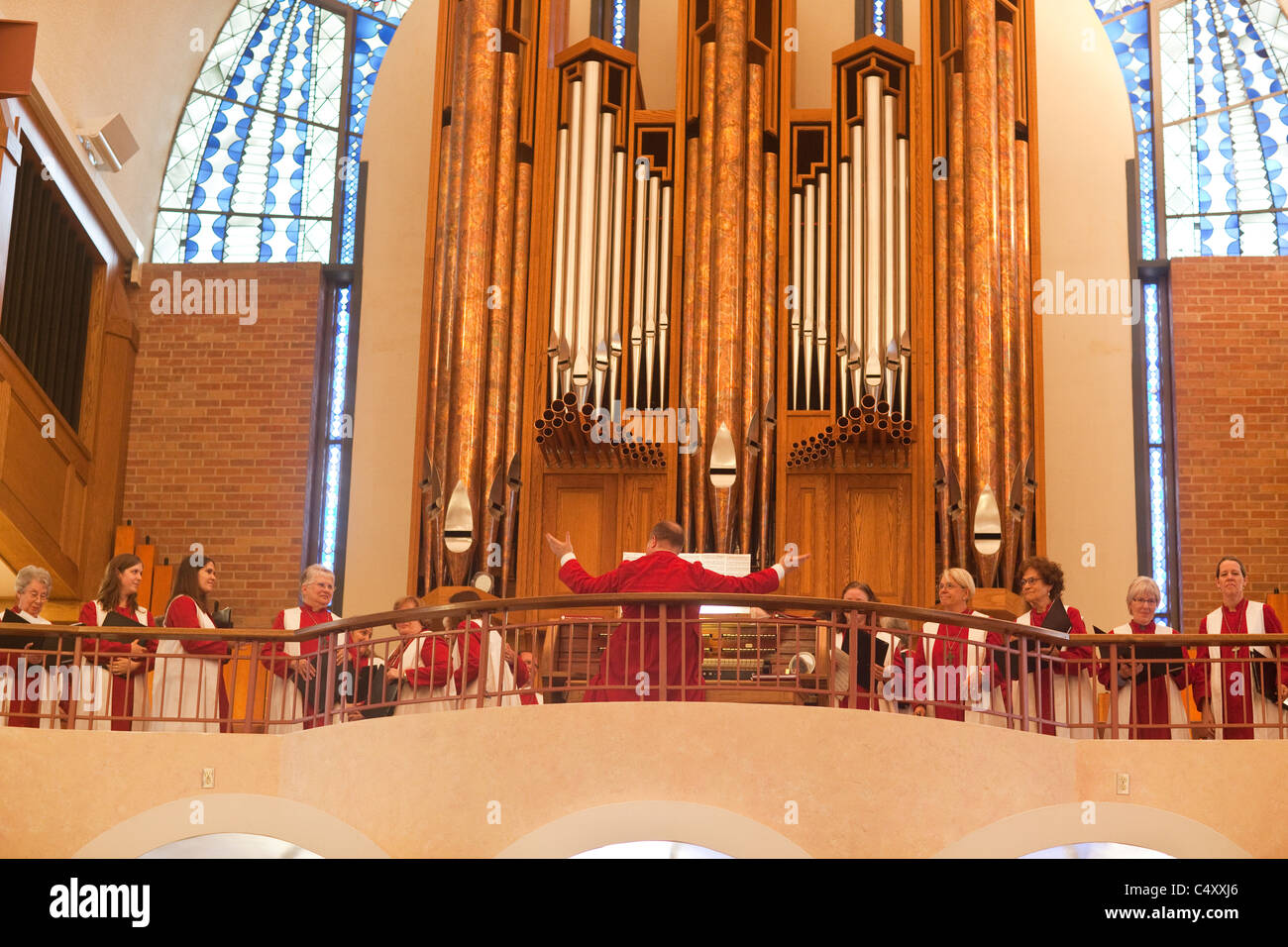 Director leads church choir in song in front of large pipe organ's ...