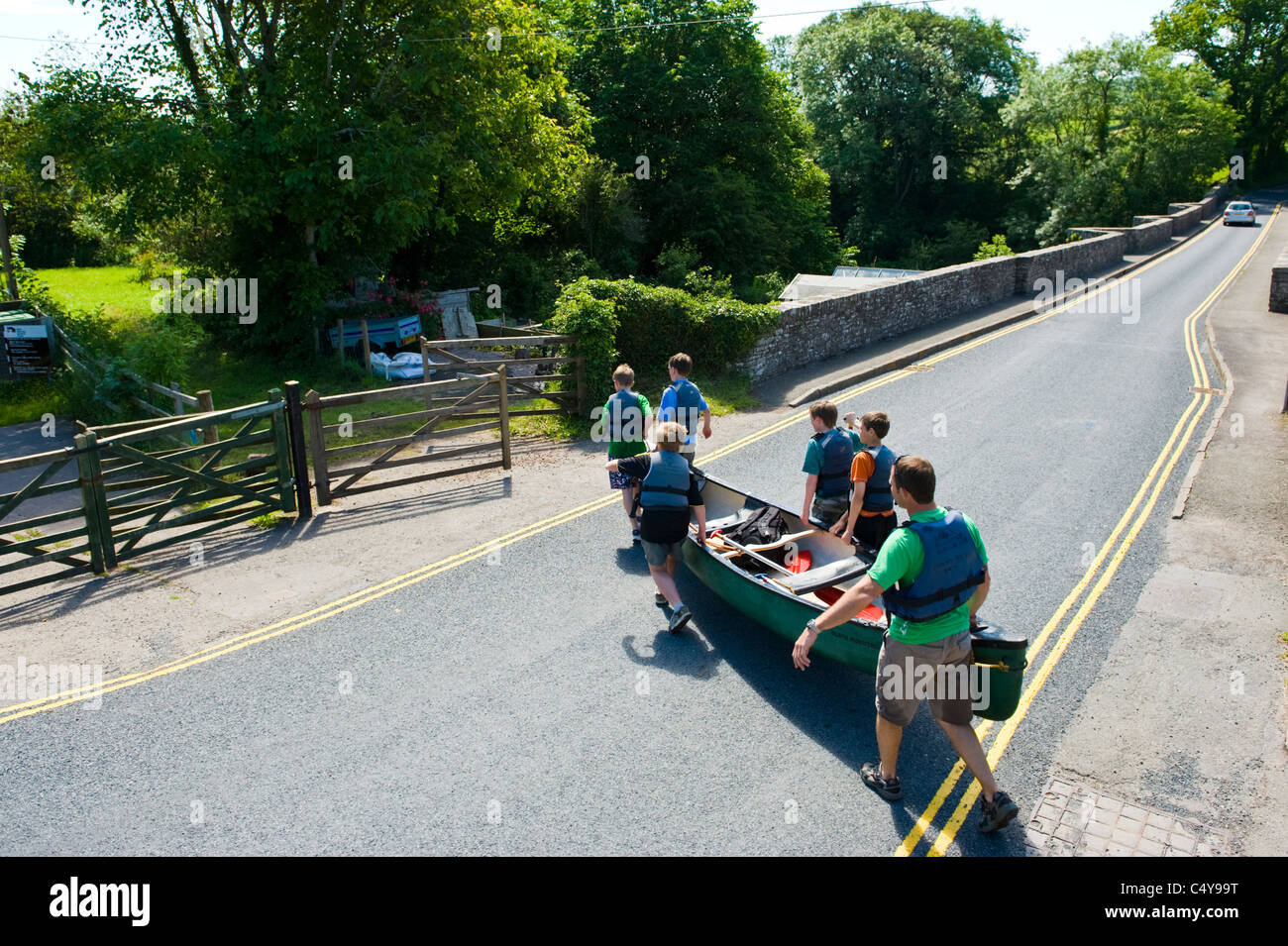 Canoeists carrying open canoe across road near Brecon Powys South Wales ...