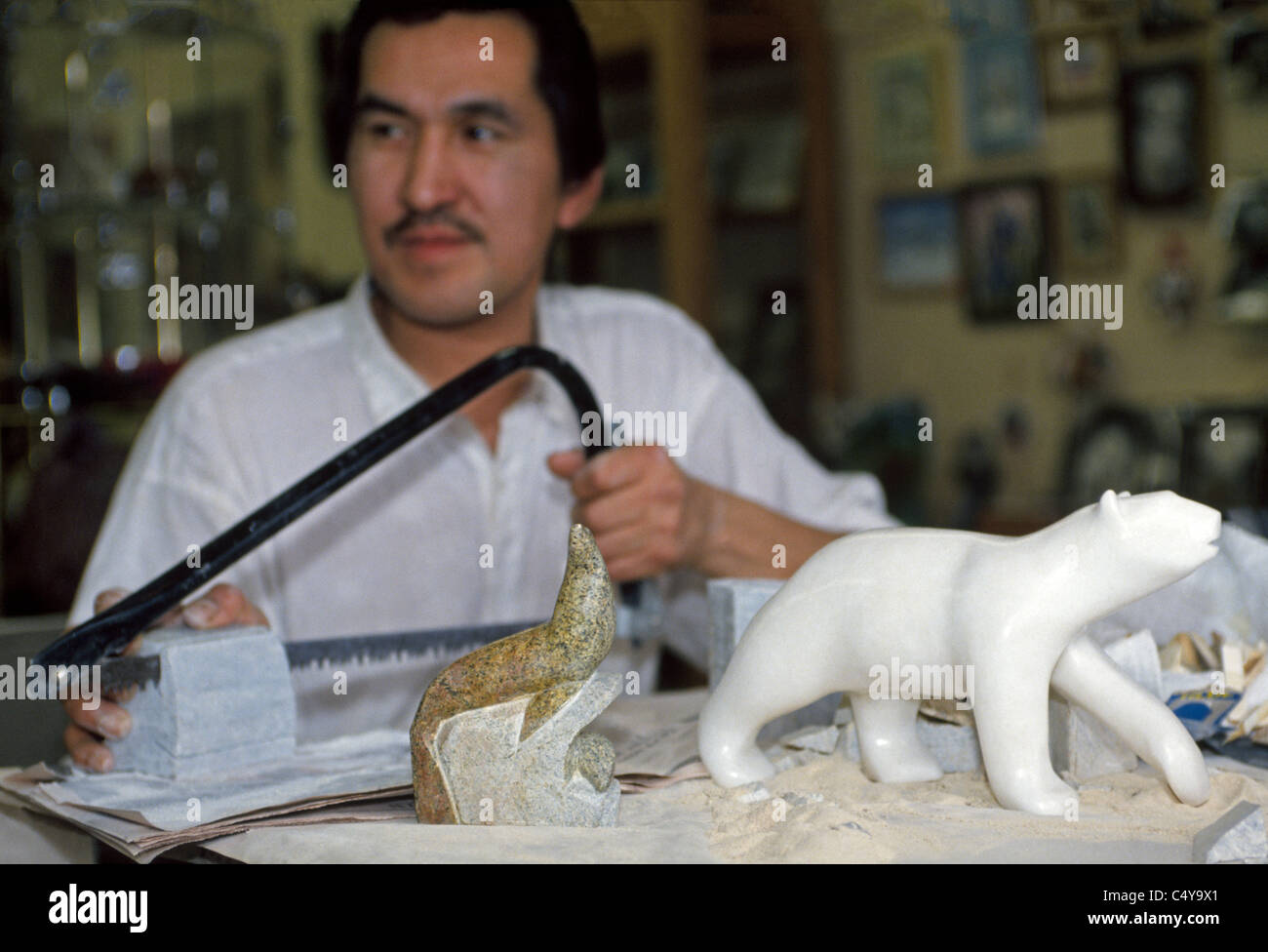 A Native Alaskan artist uses a handsaw to resize a block of stone for ...