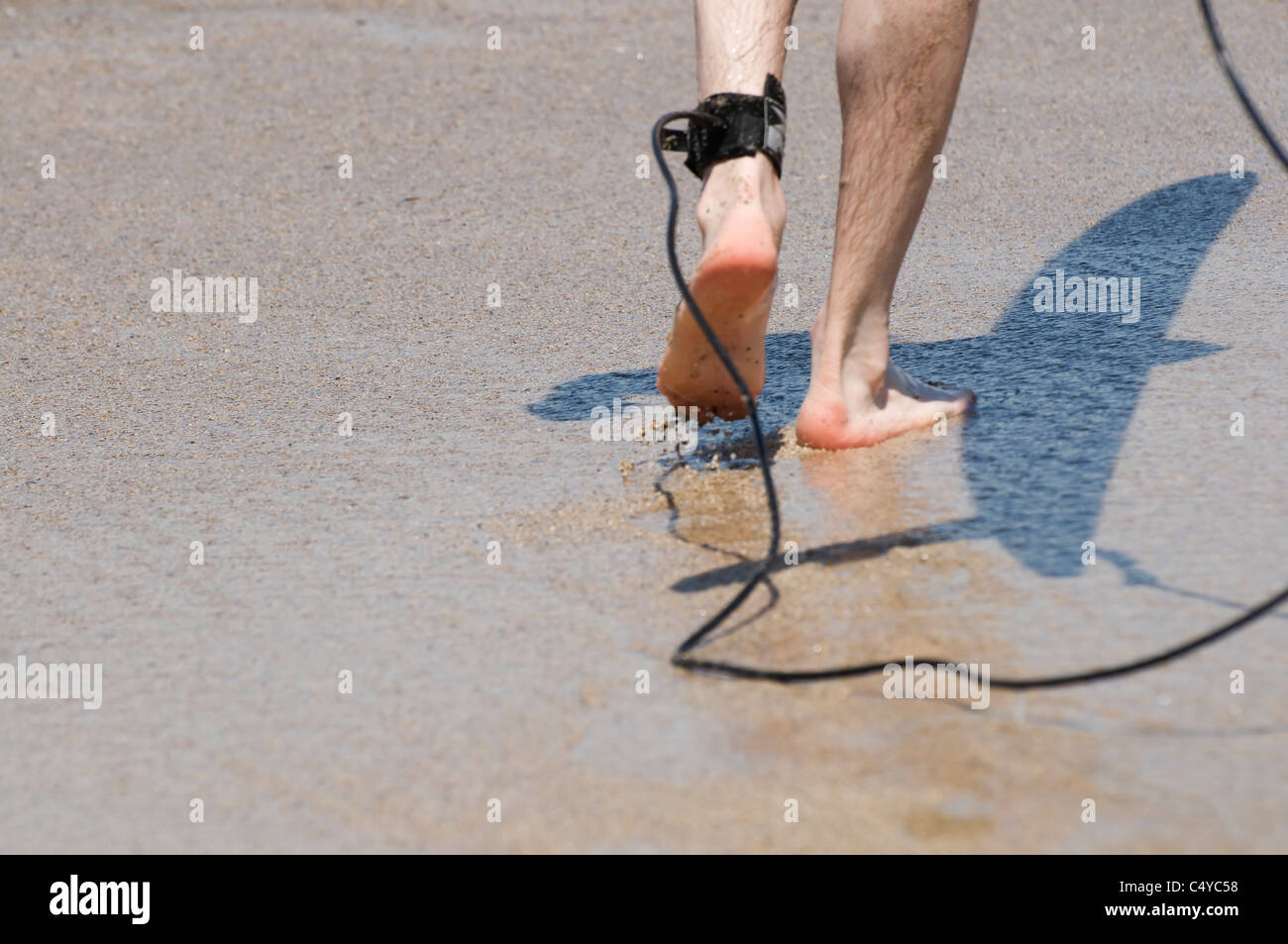 A male surfer's legs with surfboard leash attached to ankle walks away ...