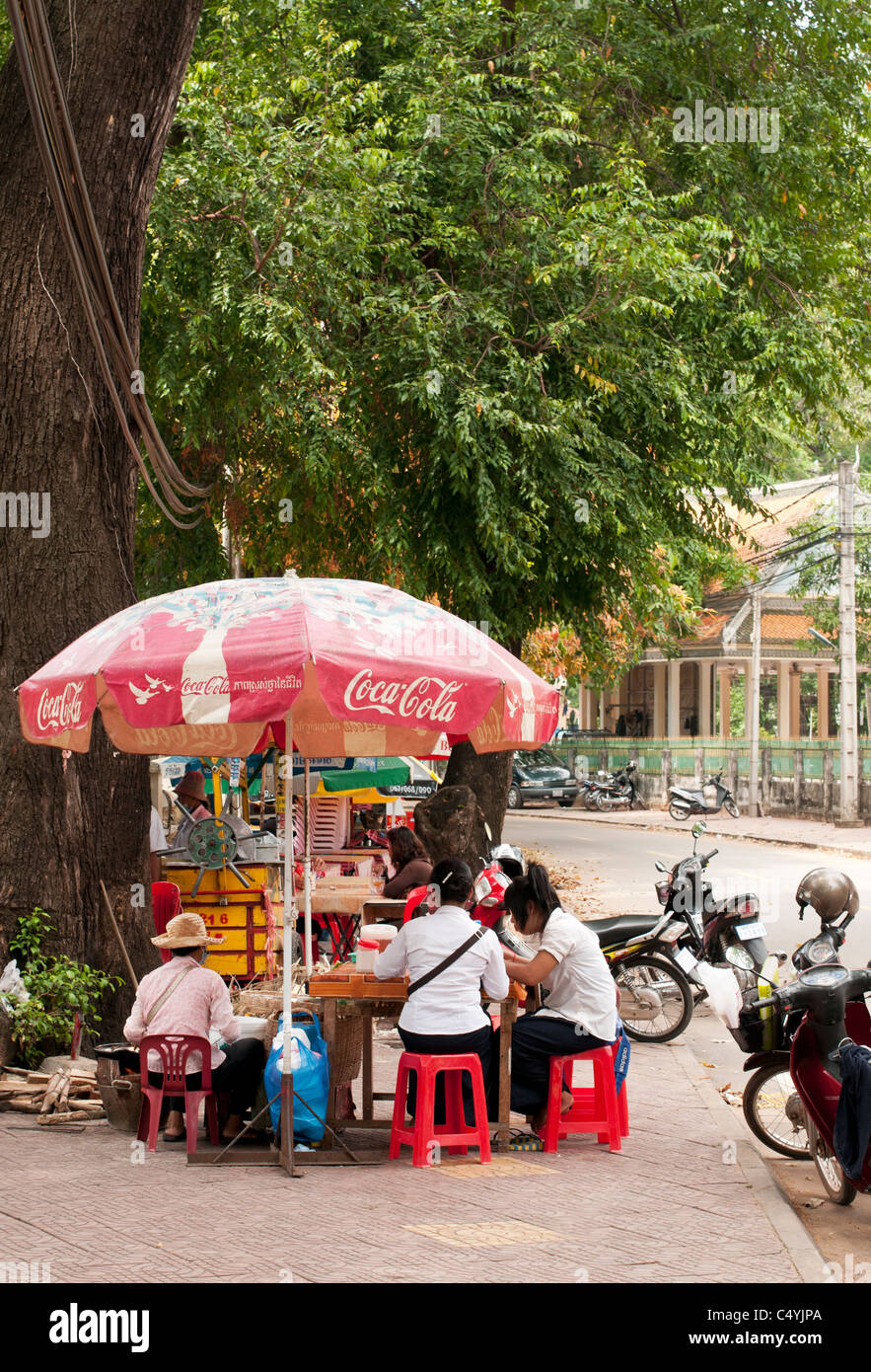 Two Cambodian schoolgirls eating at a roadside food stall, Siem Reap ...