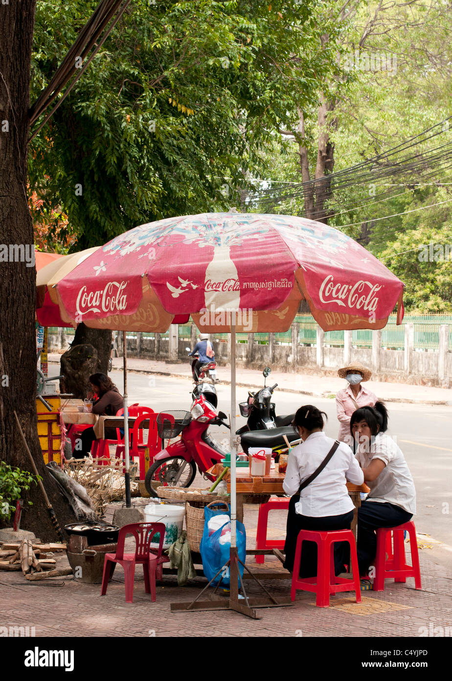 Two Cambodian schoolgirls eating at a roadside food stall, Siem Reap ...