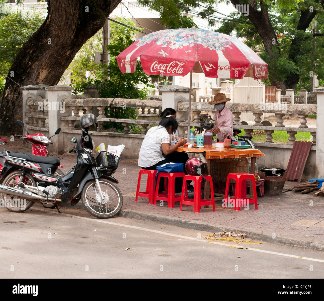 Two Cambodian schoolgirls eating at a roadside food stall, Siem Reap ...