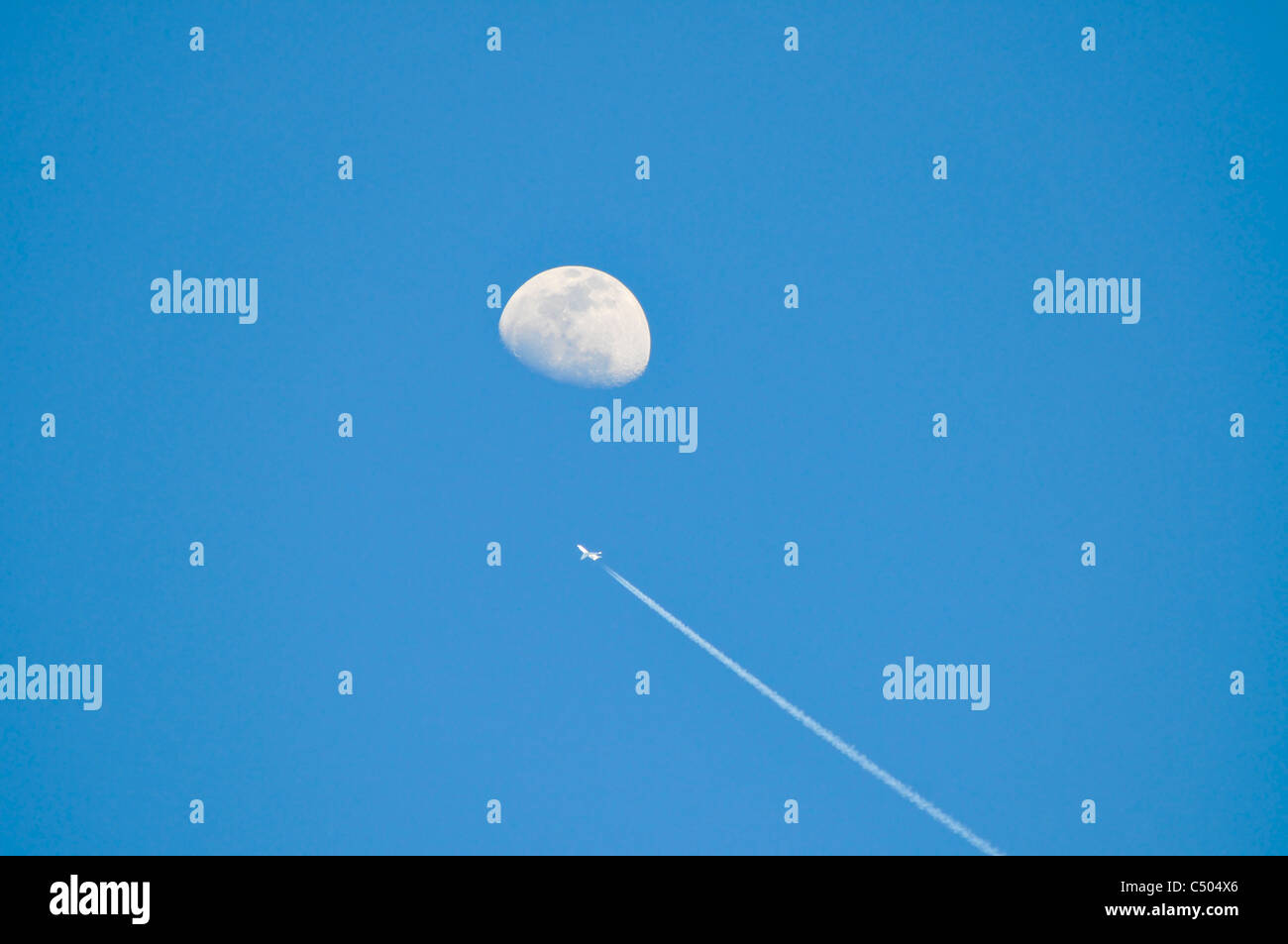 Day time moon on blue sky background A jet plane is seen crossing the ...