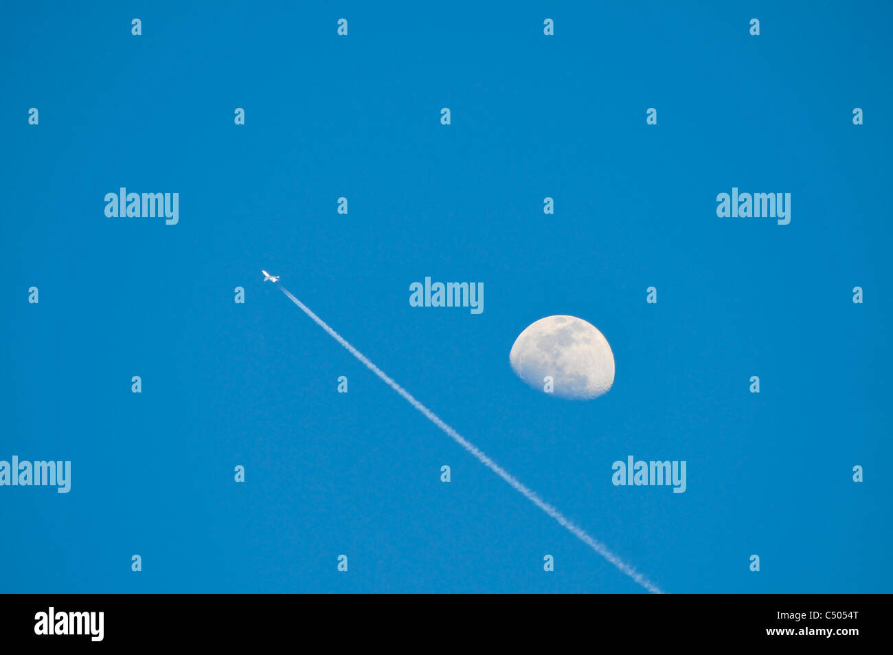 Day time moon on blue sky background A jet plane is seen crossing the ...