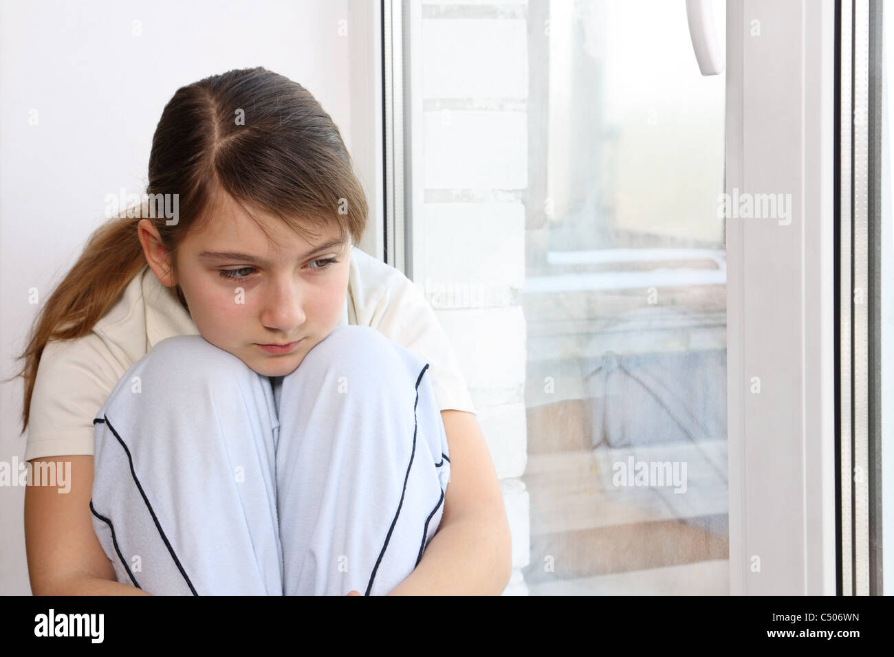 Girl sitting on the windowsill, looking out the window with a sad ...