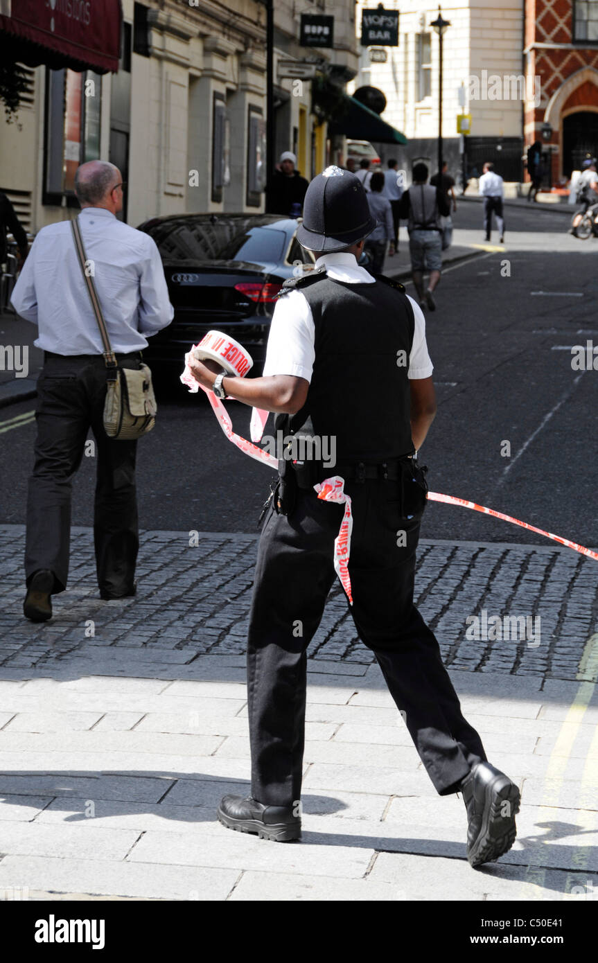 Metropolitan police officer rolling out tape to cordon off pedestrian ...