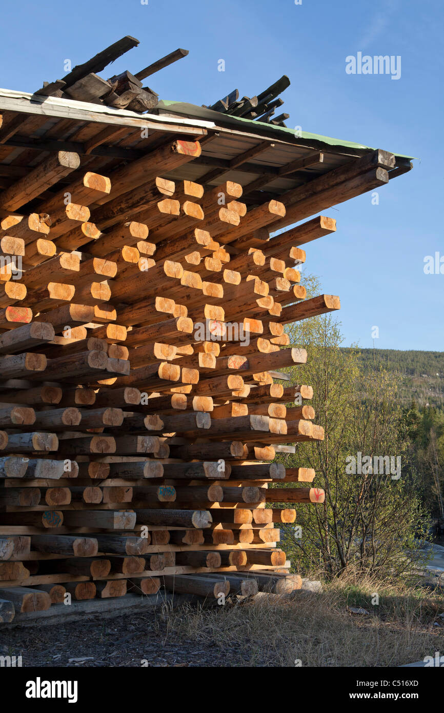 Wooden planks stacked together by a flowing river with forest and ...