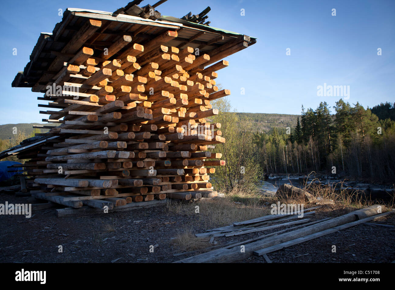 Wooden planks stacked together by a flowing river with forest and ...