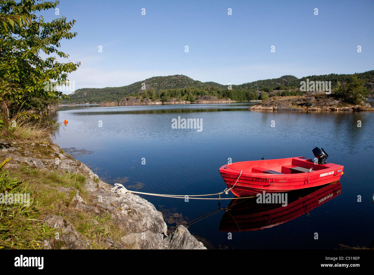 Afloat red motor boat on a calm lake tied to rocky shore, with the ...