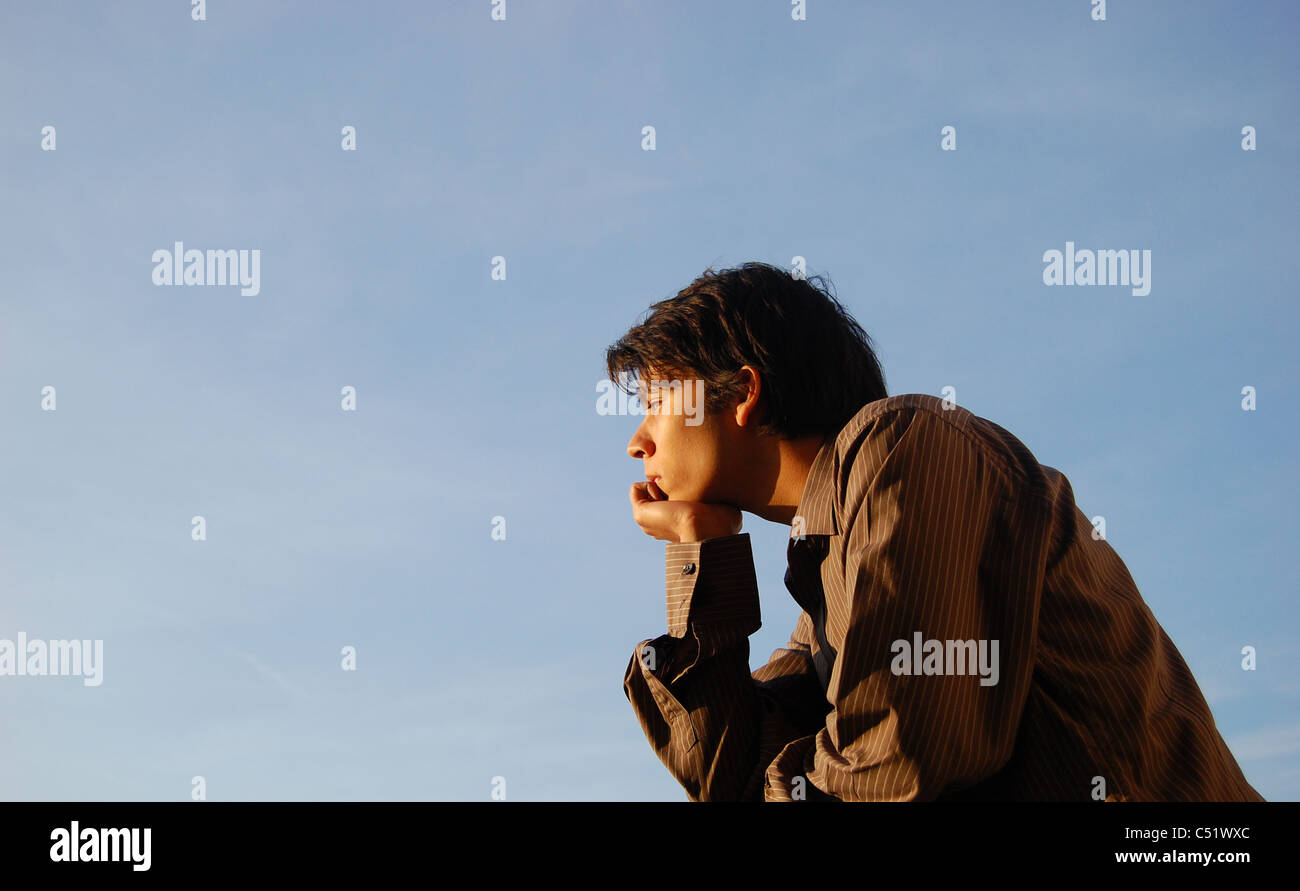 Young man daydreaming gazing staring thinking contemplating blue sky in ...