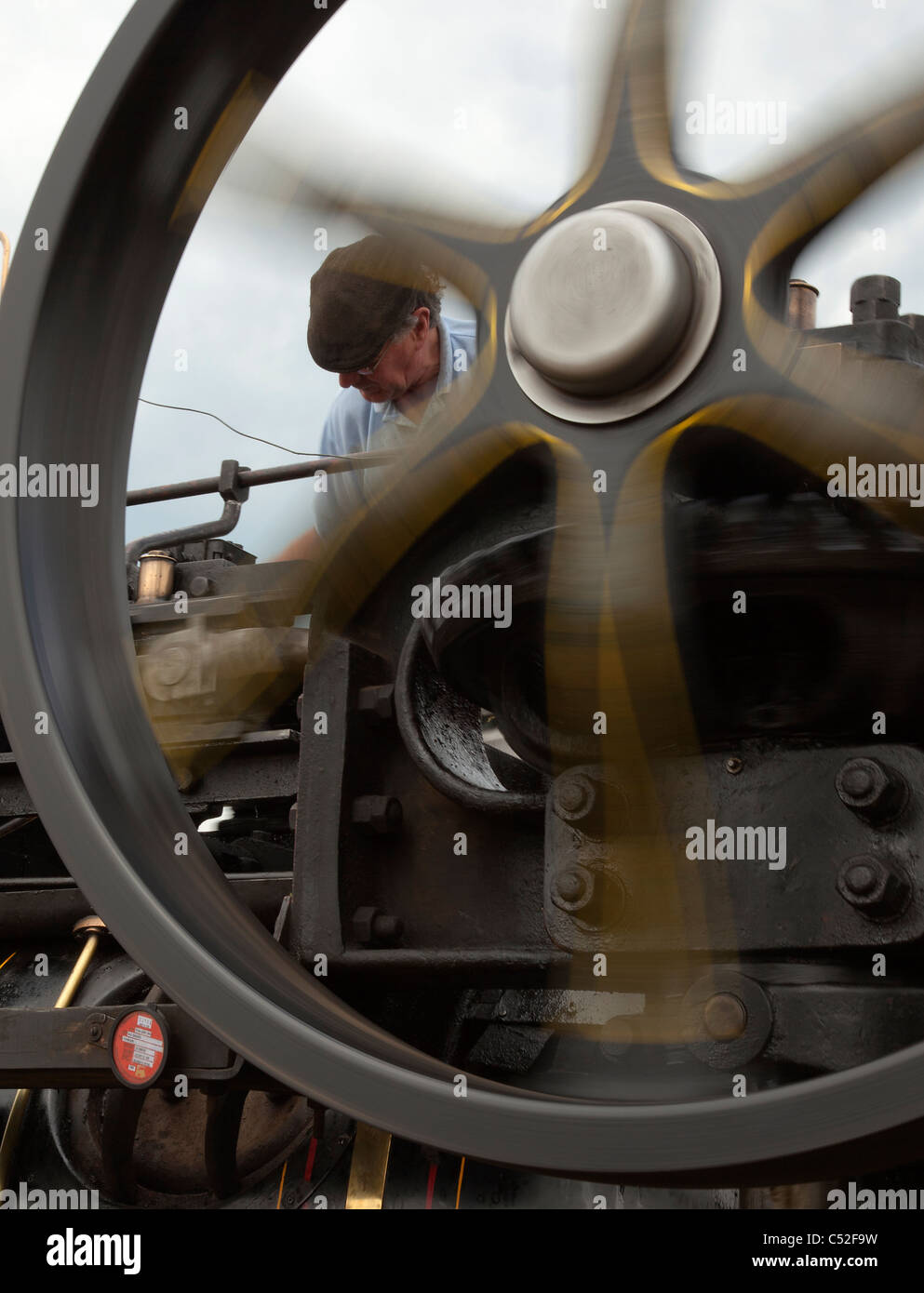 Engineer seen through spinning flywheel of a steam traction engine ...