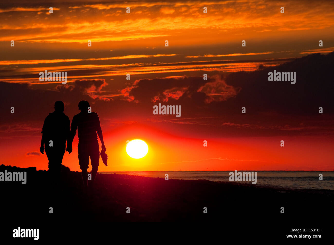 Couple walking hand in hand along a beach at sunset, on the Norfolk ...
