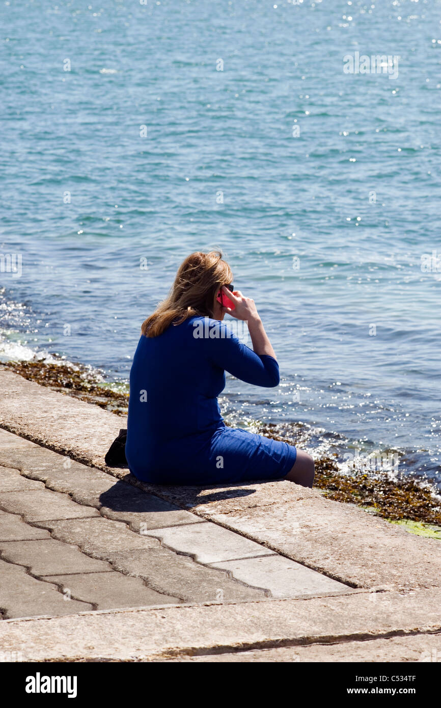 lone woman sitting on seafront using mobile telephone Stock Photo - Alamy