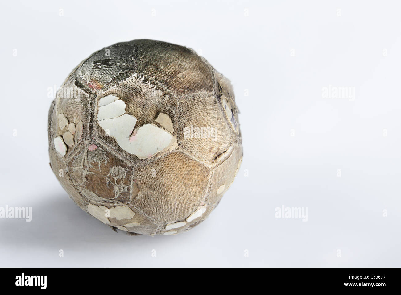 worn out soccer ball on white surface, suggests old, poor or historic ...
