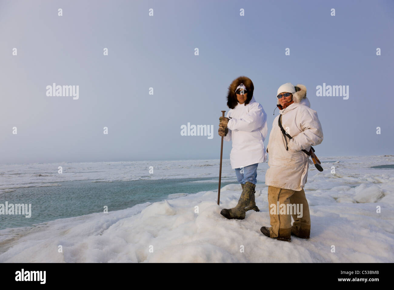 Inupiaq Eskimo hunters in parkas carry a rifle and walking stick while ...
