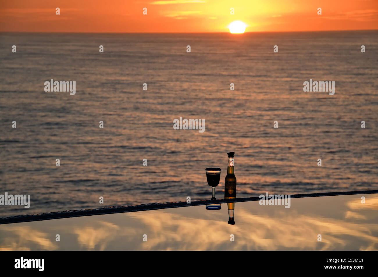 A glass of wine and a bottle of beer are placed on the edge of an ...